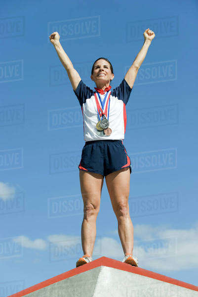 Female athlete standing on winner's podium with arms raised in victory ...
