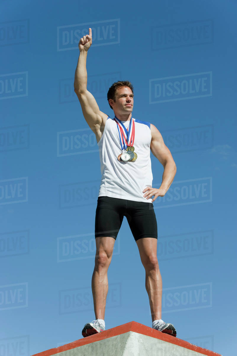 Male athlete standing on winner's podium with hand raised in victory ...