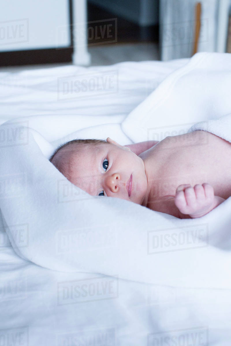 Newborn baby lying on bed, looking at camera - Royalty-free Stock Photo | Dissolve