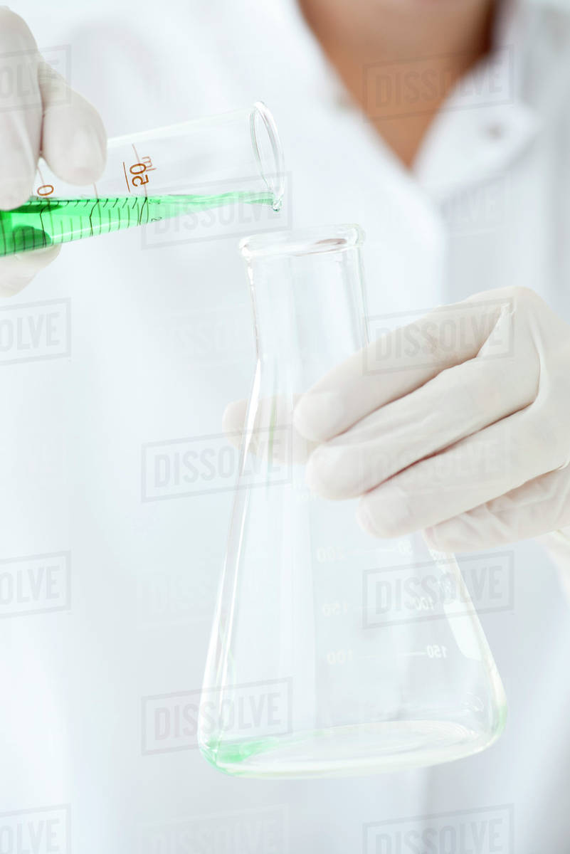 Scientist pouring liquid from graduated cylinder to conical flask ...