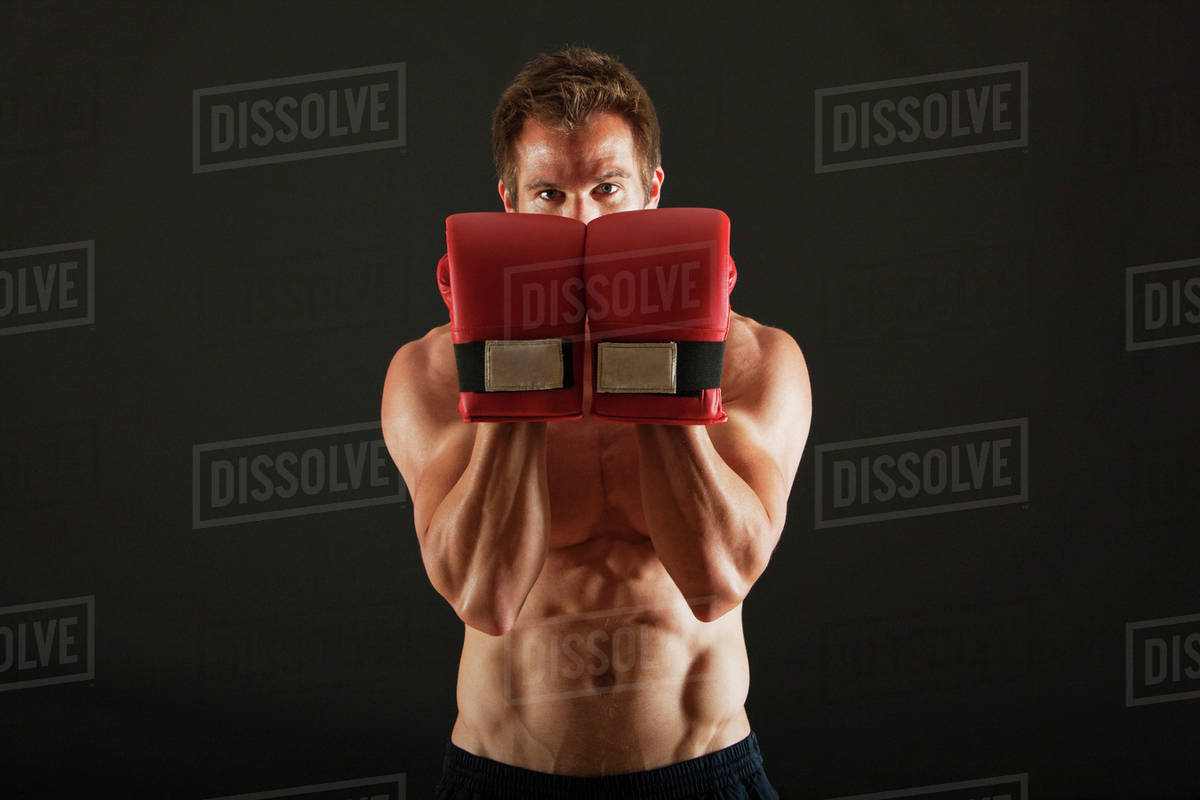 Barechested boxer holding up gloves in front of face in defensive ...