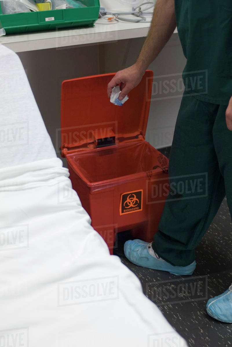 Healthcare professional putting trash in biohazard waste receptacle ...