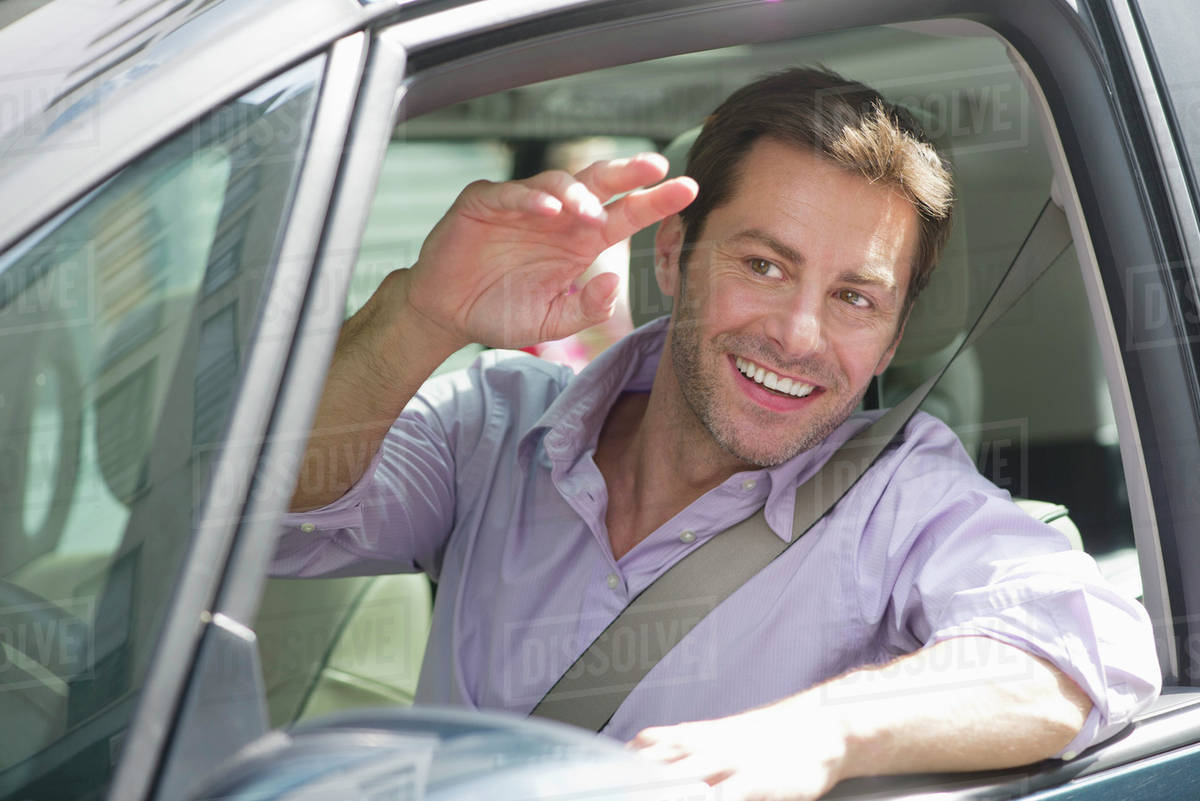 Man driving car, smiling out window and waving - Stock Photo - Dissolve