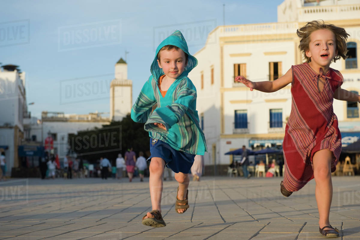 Young siblings running together on sidewalk - Stock Photo - Dissolve