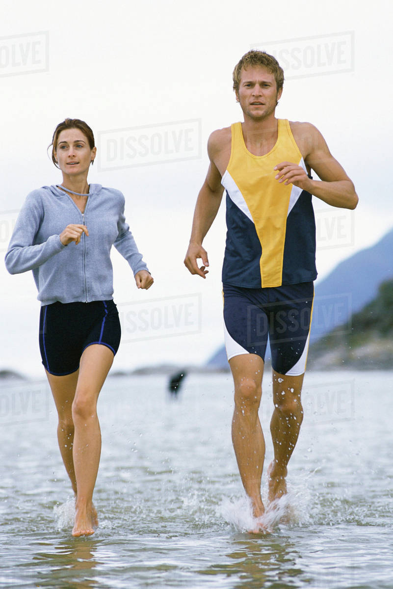 Young couple running together through shallow water near shore - Stock ...
