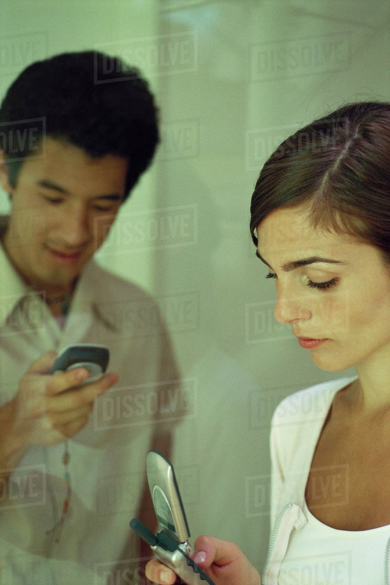 Young woman looking at cell phone, man in background lookng at own ...