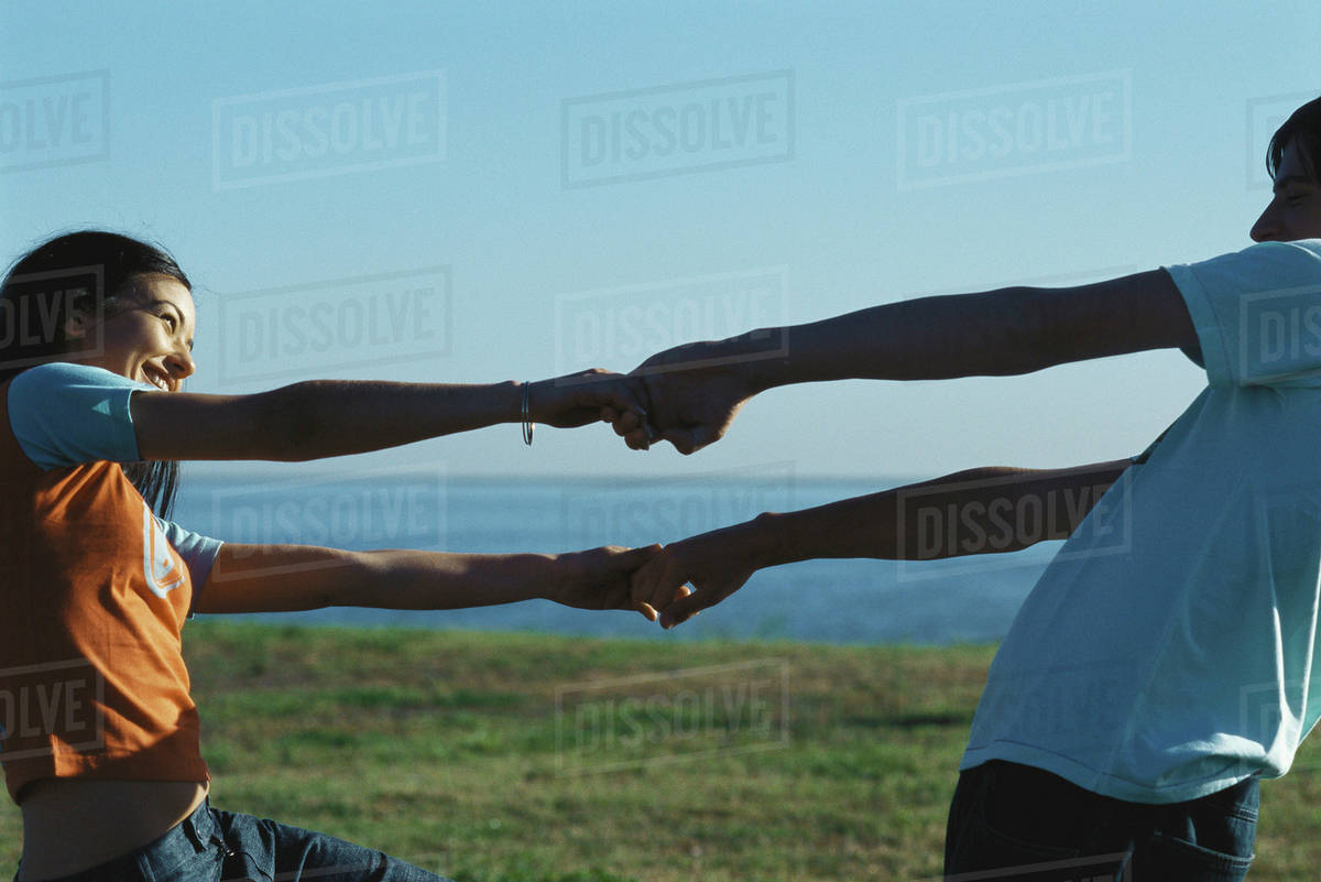 Young couple facing one another holding hands and leaning back smiling ...