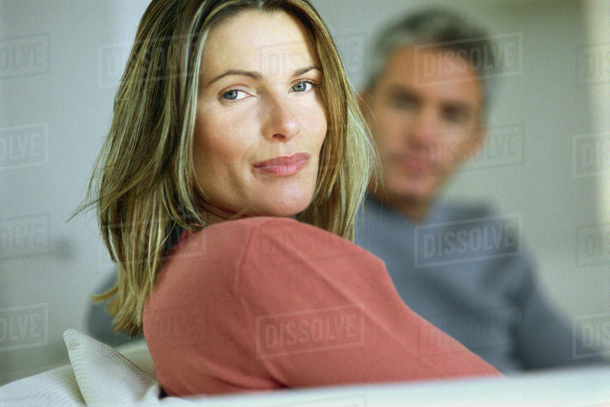 Woman smiling over shoulder at camera, man in background - Stock Photo ...