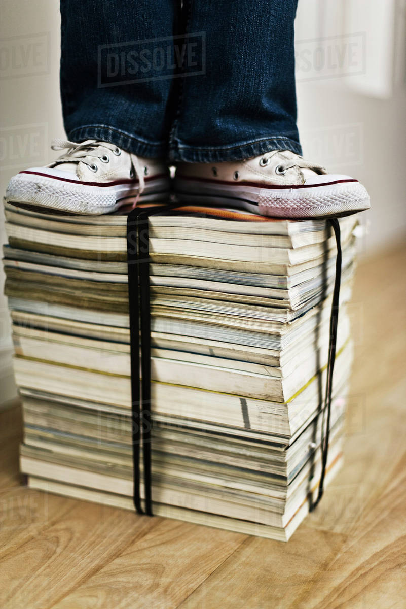 Person standing on top of bound stack of books and magazines - Royalty ...