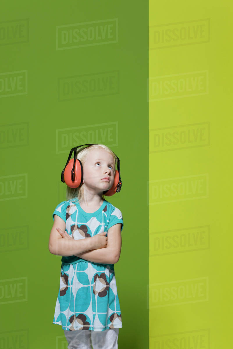 Little girl with arms folded, wearing protective headphones, defiantly ...