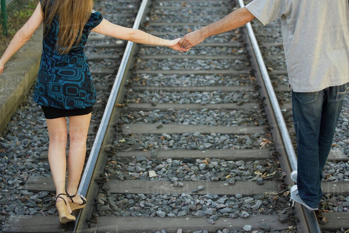 Young couple holding hands walking on rail track, rear view - Royalty ...