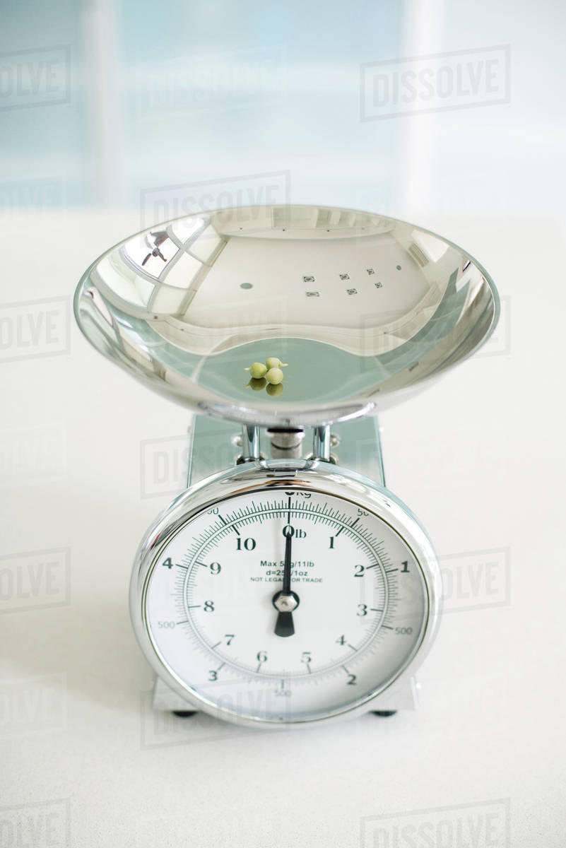 Three capers on scale, close-up - Stock Photo - Dissolve