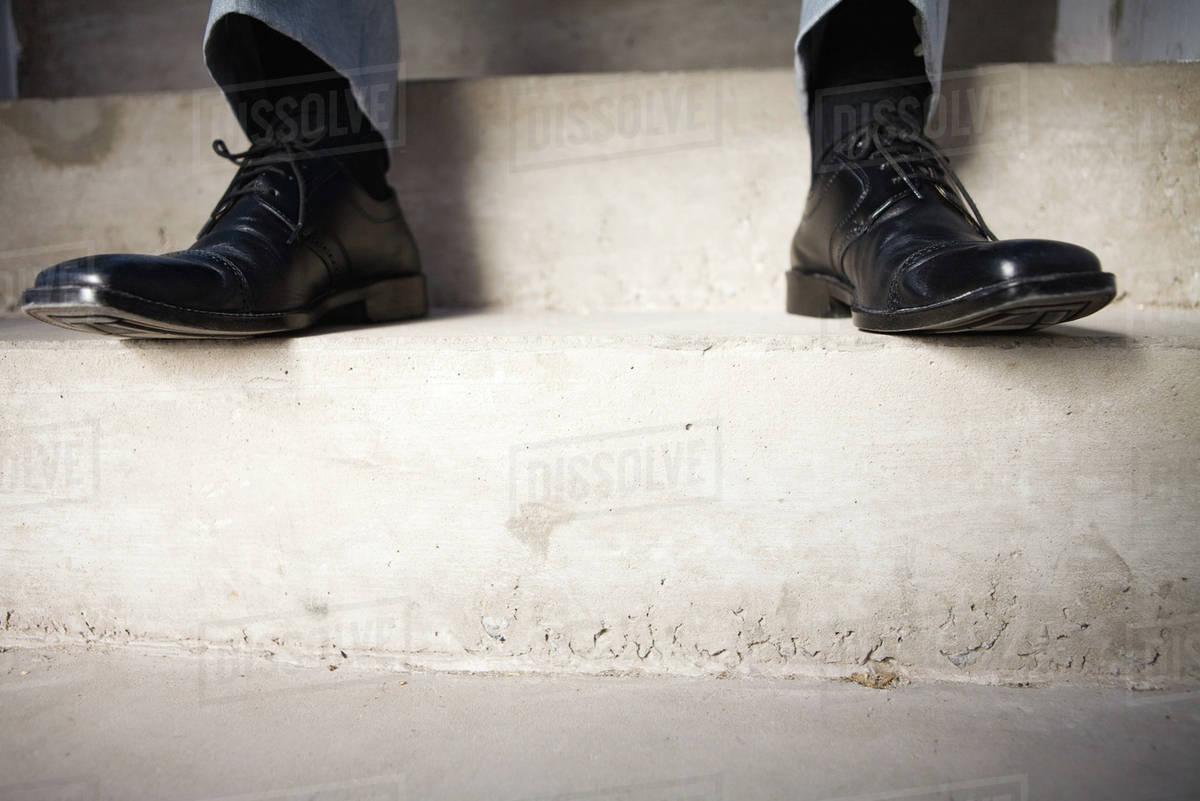 Businessman sitting on steps, cropped view of feet, low angle view ...