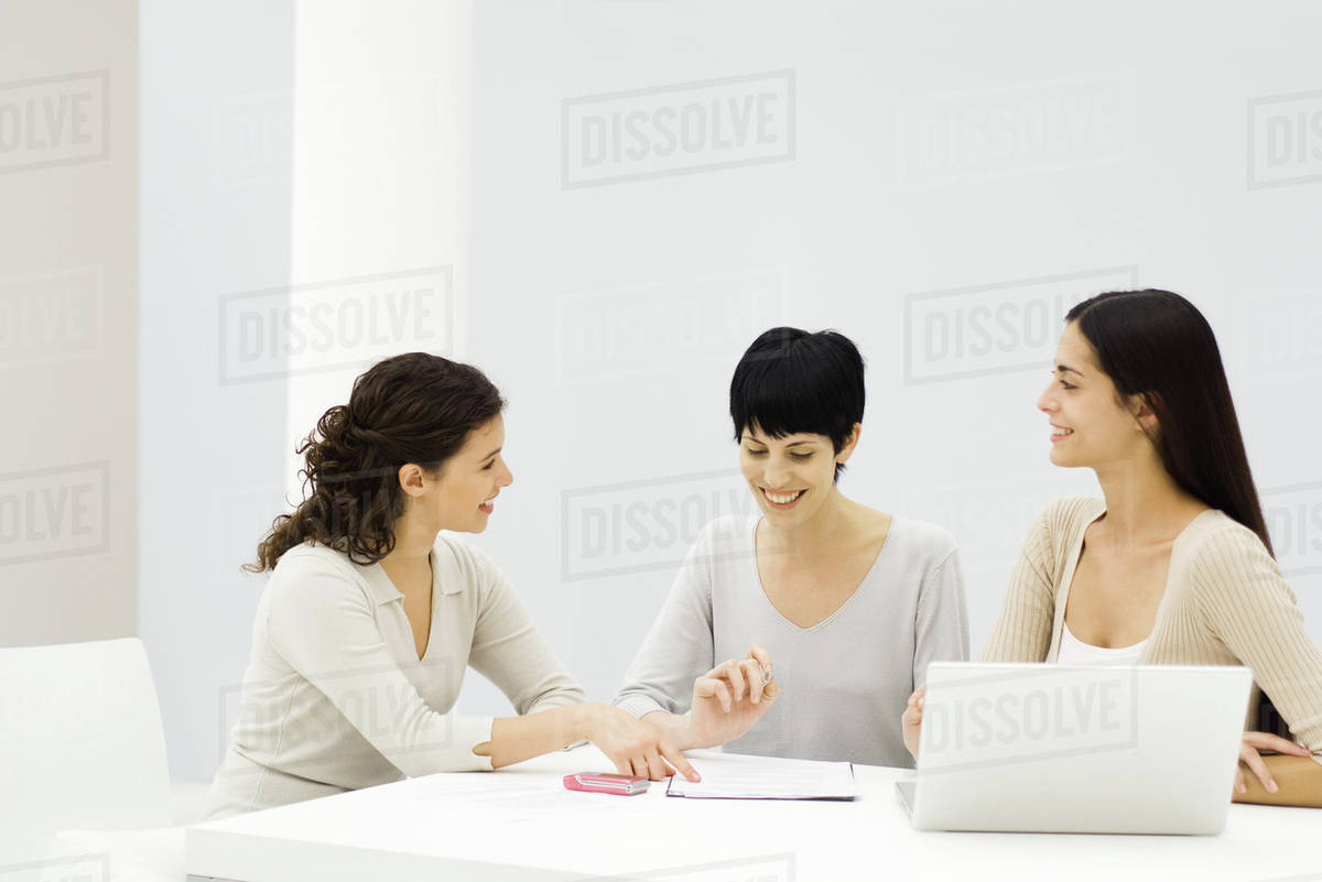 Three businesswomen sitting at table, discussing document, smiling ...