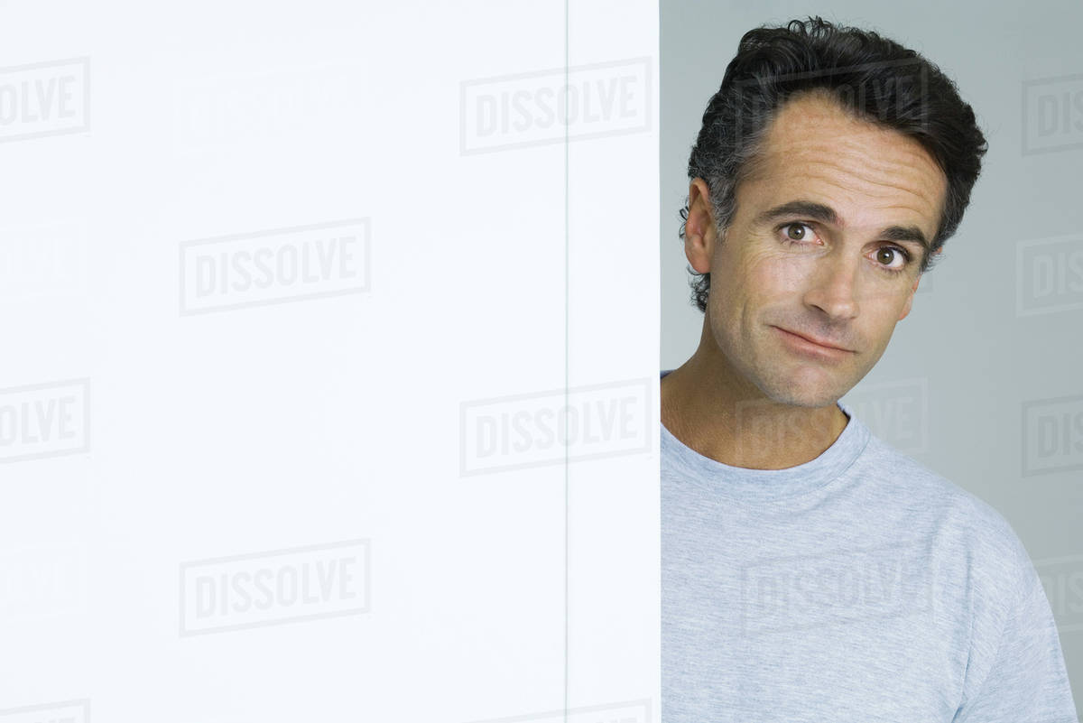 Man looking around corner of wall, portrait - Stock Photo - Dissolve