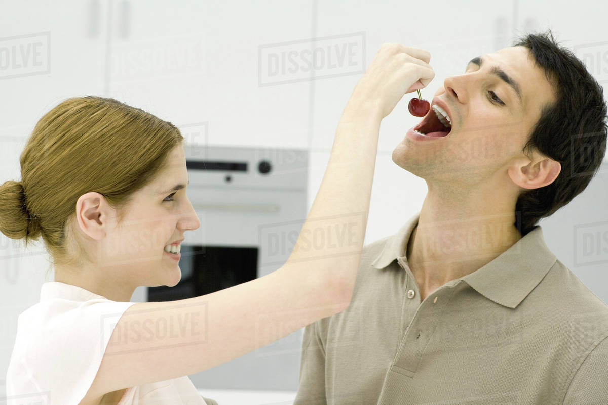 Young couple in kitchen, woman feeding man cherry - Royalty-free Stock ...