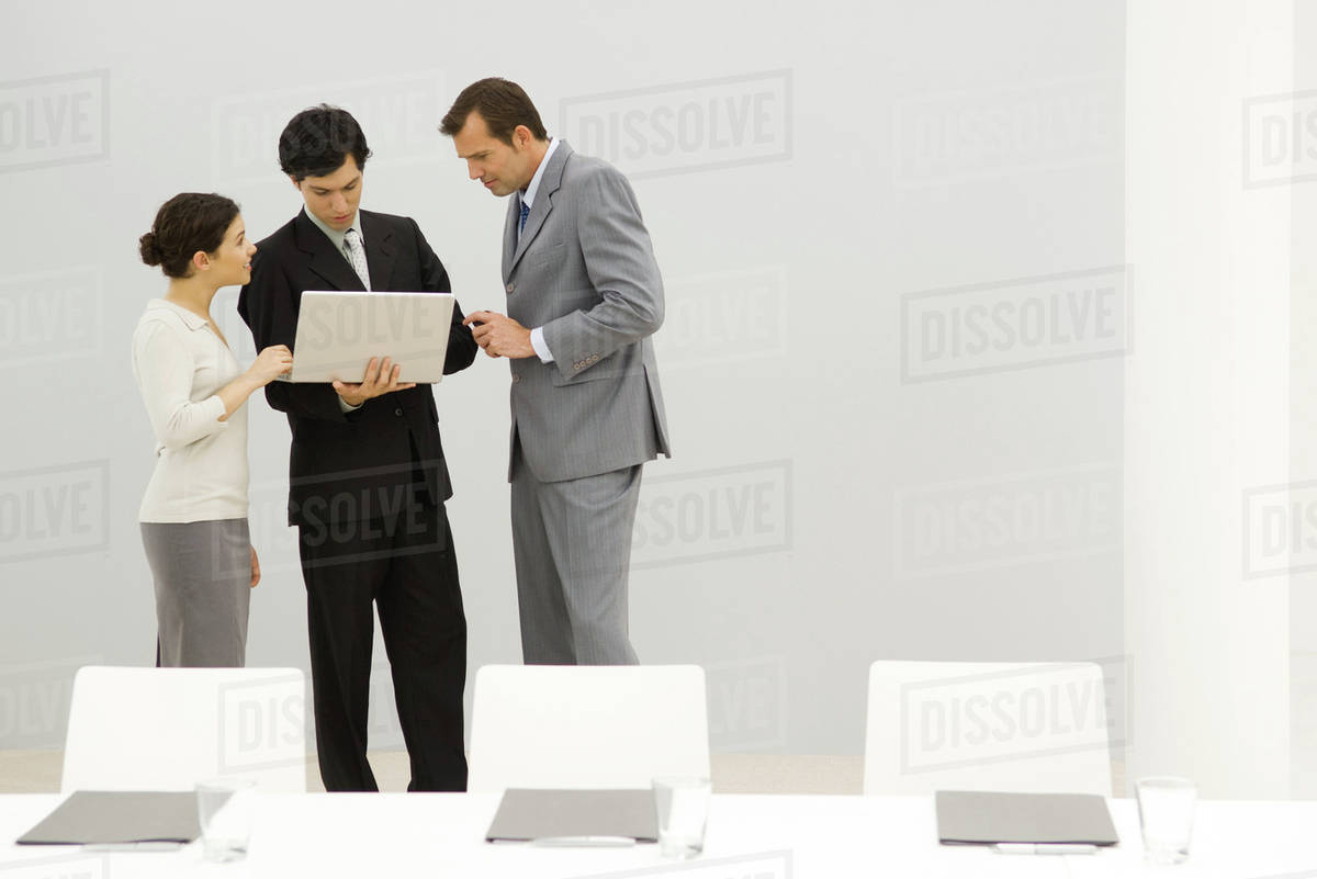 Business associates standing in conference room, looking at laptop ...