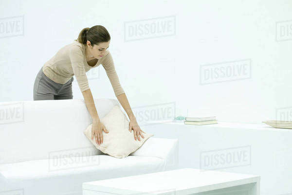 Woman leaning over couch, arranging pillow - Royalty-free Stock Photo ...