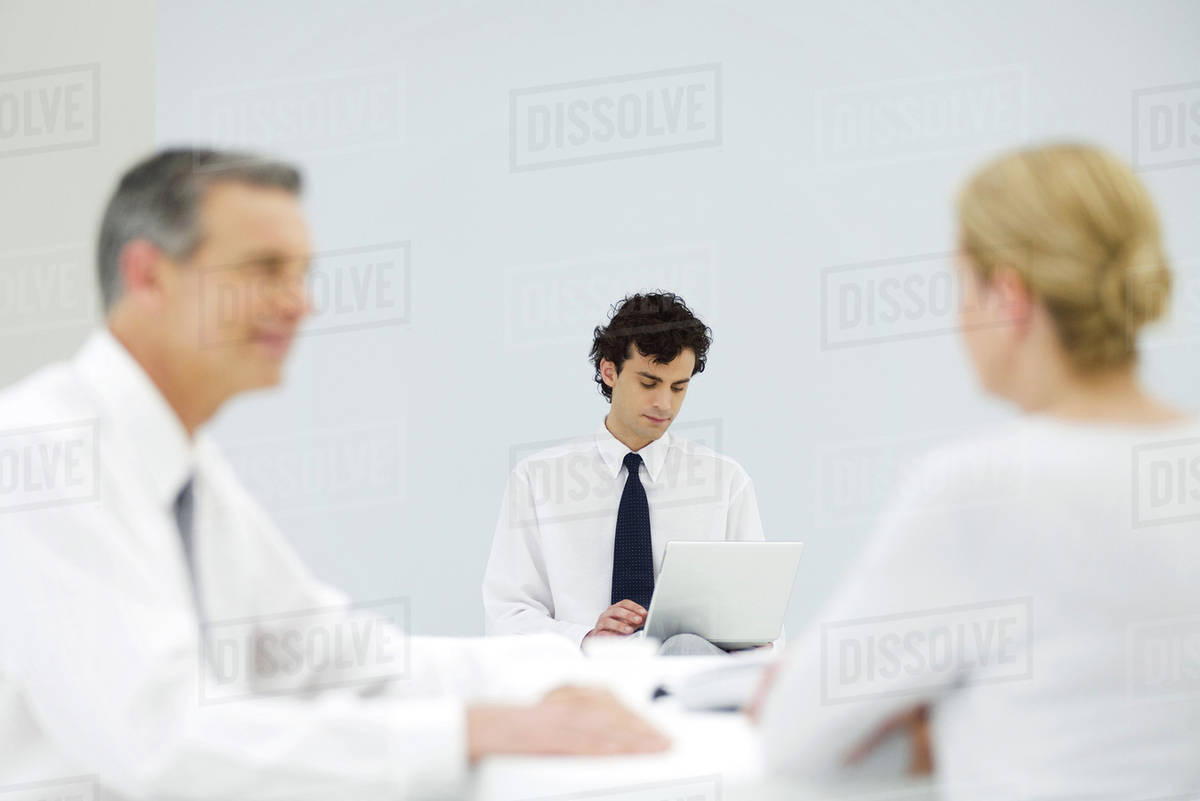 Male professional using laptop computer, colleagues talking in ...