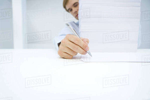 Man sitting behind tall stack of documents, writing on single sheet of ...