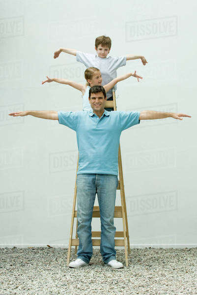 Family standing on ladder with arms out, girl looking away, father and ...