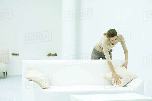 Woman leaning over couch, arranging pillow - Stock Photo - Dissolve