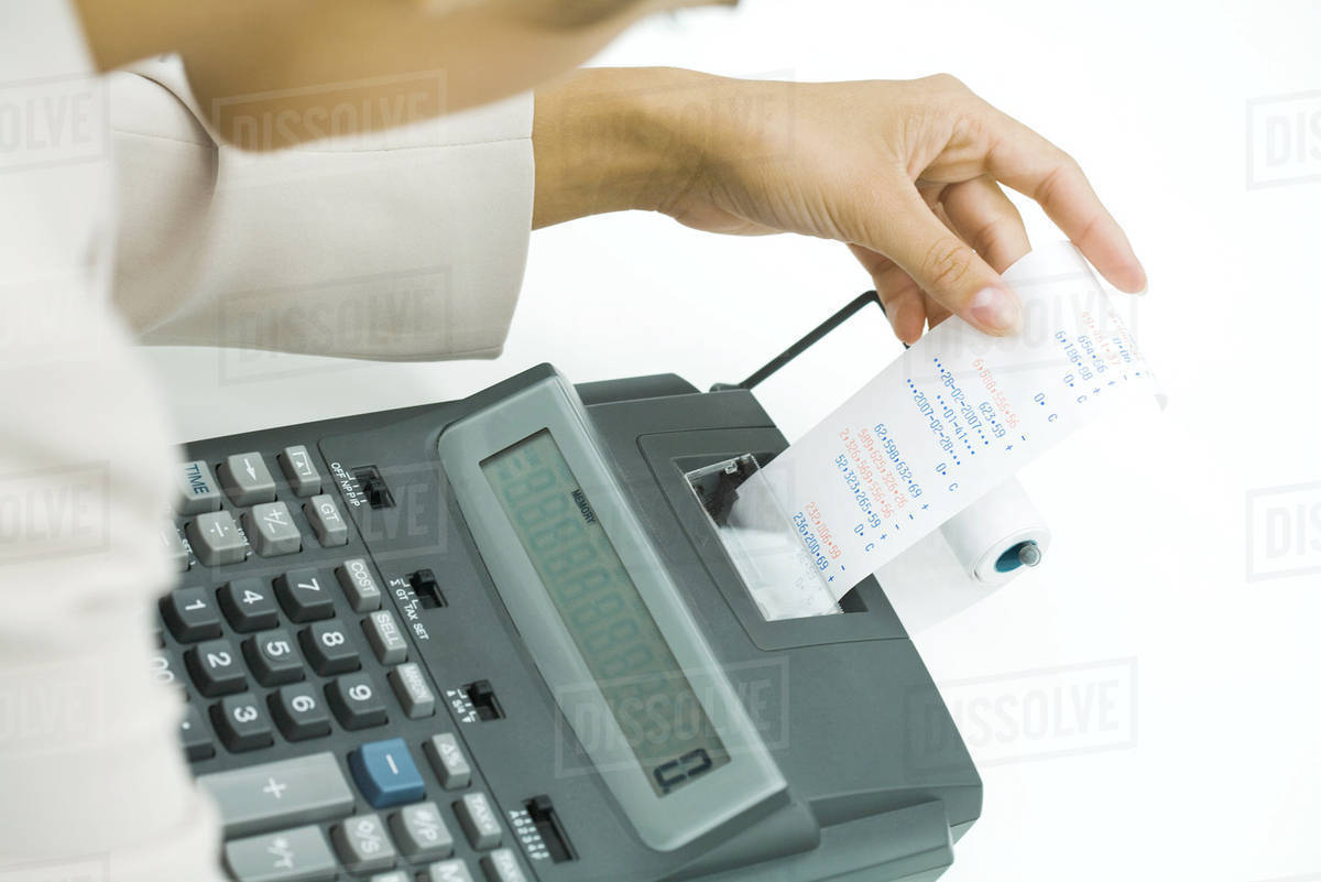 Businesswoman using adding machine, holding printout, cropped view ...