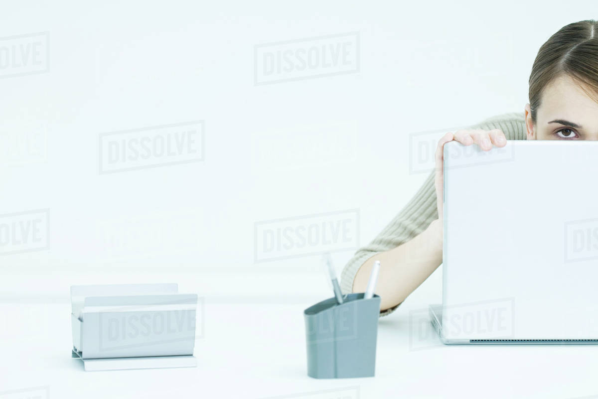 Young woman peeking over laptop, cropped view - Stock Photo - Dissolve