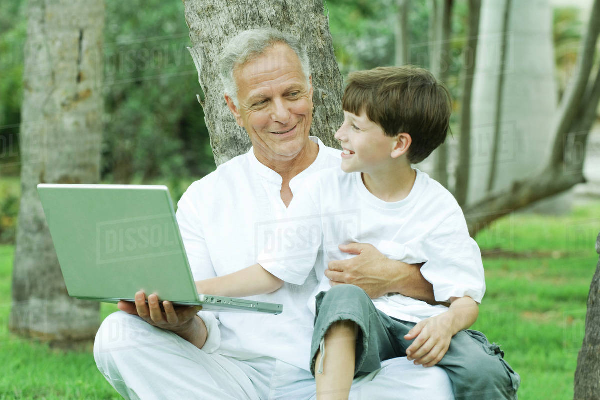 Grandfather holding grandson on lap, boy looking at laptop computer ...