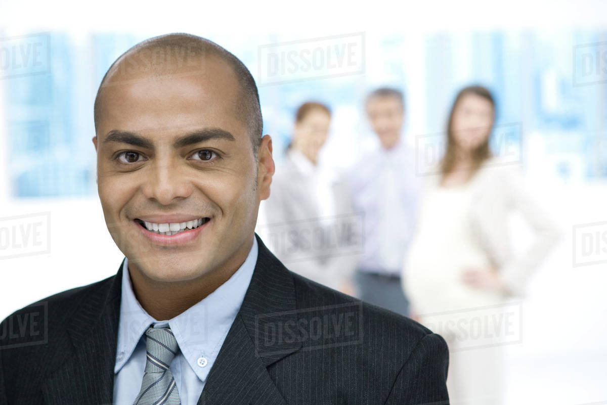 Business executive smiling at camera, colleagues standing in background ...