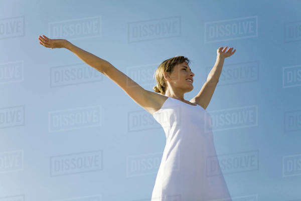 Woman standing outdoors with arms raised, smiling, low angle view ...