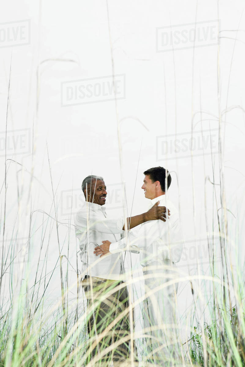 Two men facing each other in tall grass, smiling, embracing - Royalty ...