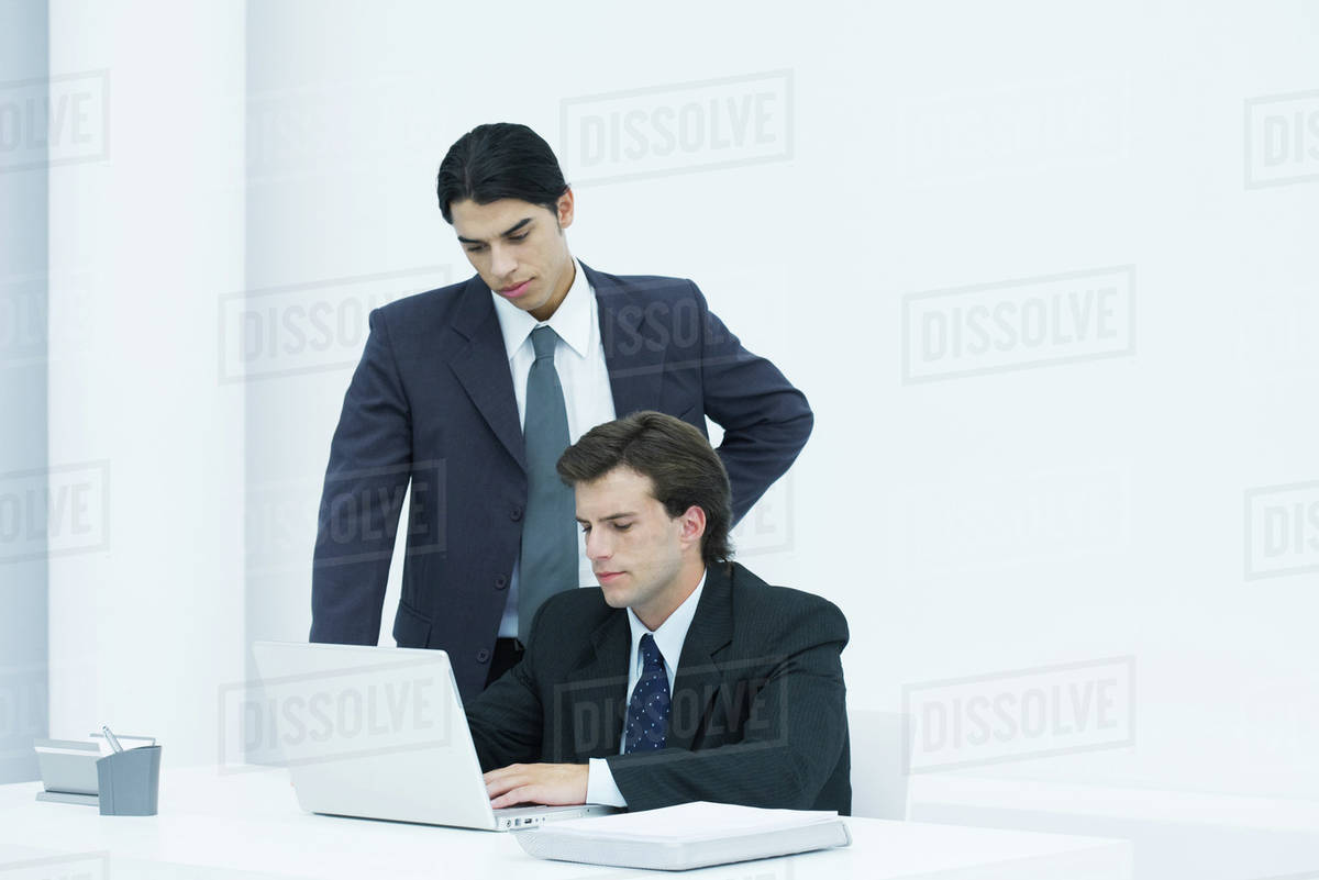 Businessman using laptop computer at desk, colleague watching over his ...