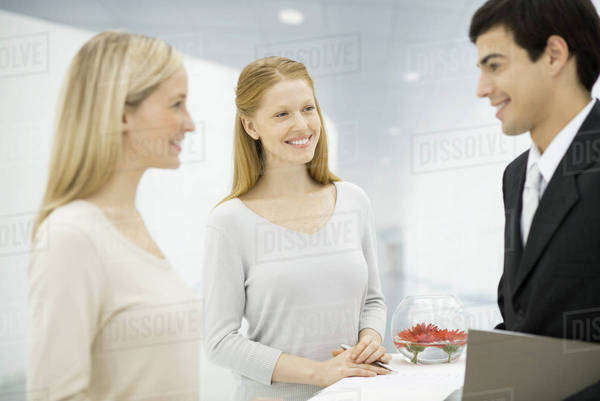 Businessman talking with two receptionists at counter, focus on women ...