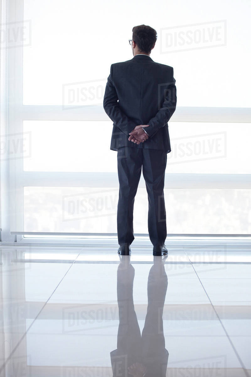 Businessman looking out high rise window at view of city below, rear ...
