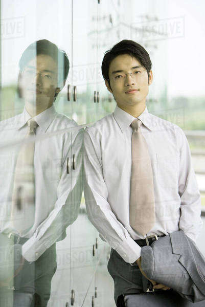 Businessman leaning against glass wall, portrait - Stock Photo - Dissolve