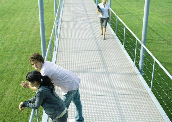 Teenage couple leaning against rail of walkway while businesswoman ...