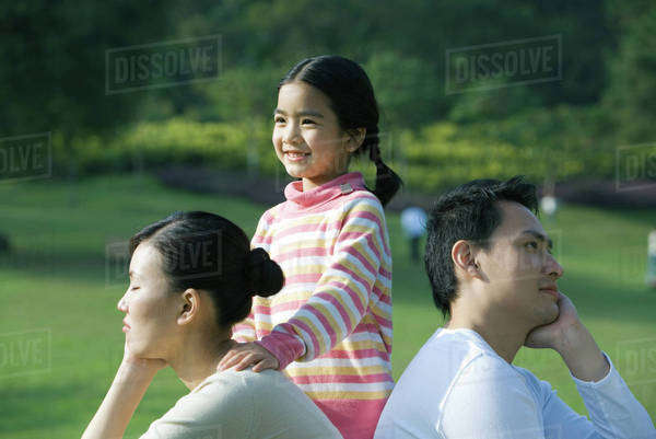 Couple sitting back to back, daughter standing behind them with hand on ...