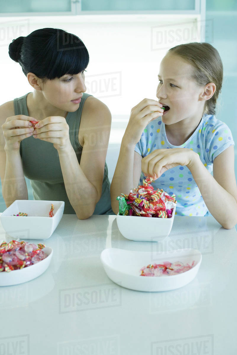 Woman and girl sitting side by side eating bowls of candy - Stock Photo ...