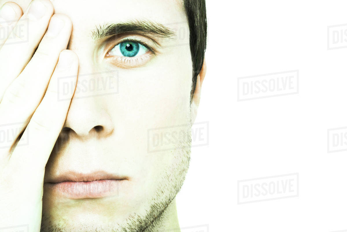 Young man covering one eye, looking at camera, extreme close-up ...