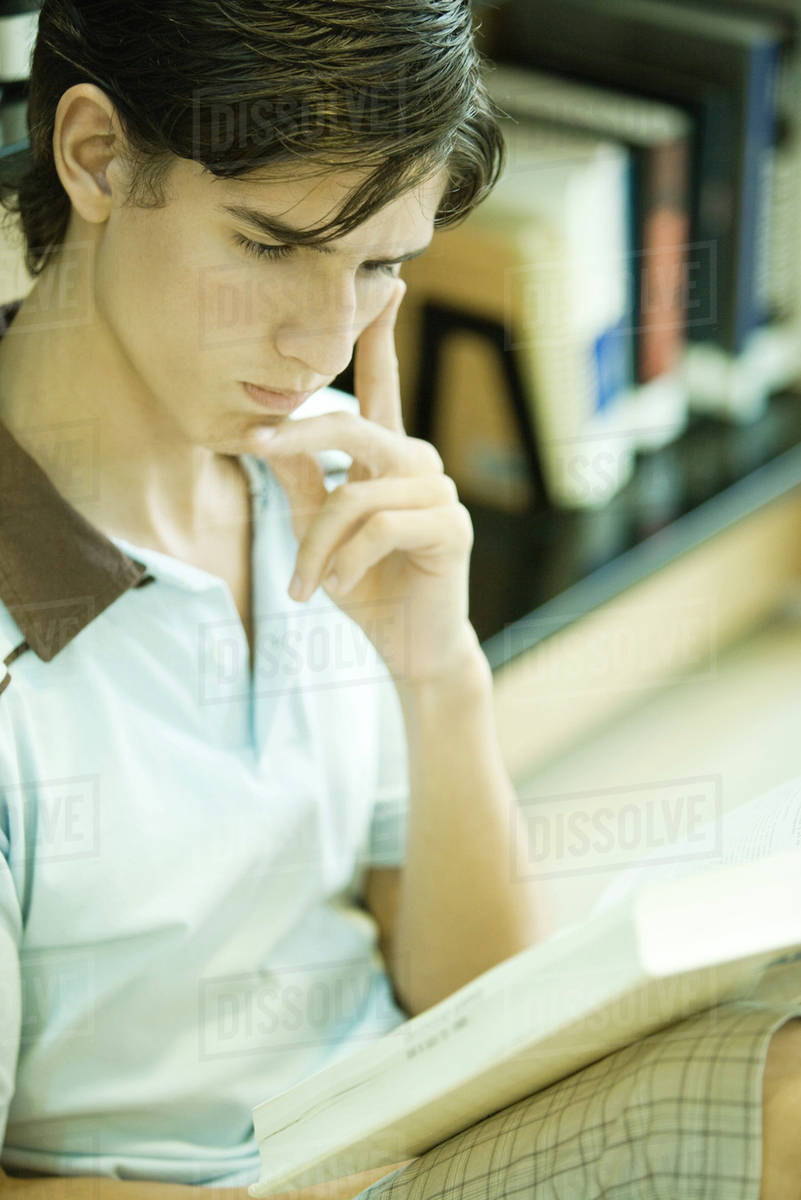 Young man sitting next to shelves of books in library, studying ...
