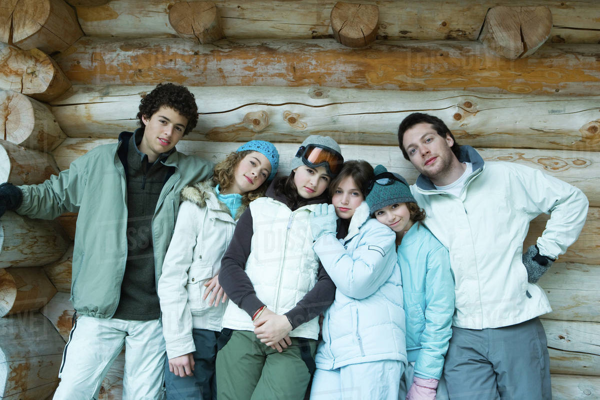 Group in winter clothes standing together, leaning against log wall ...