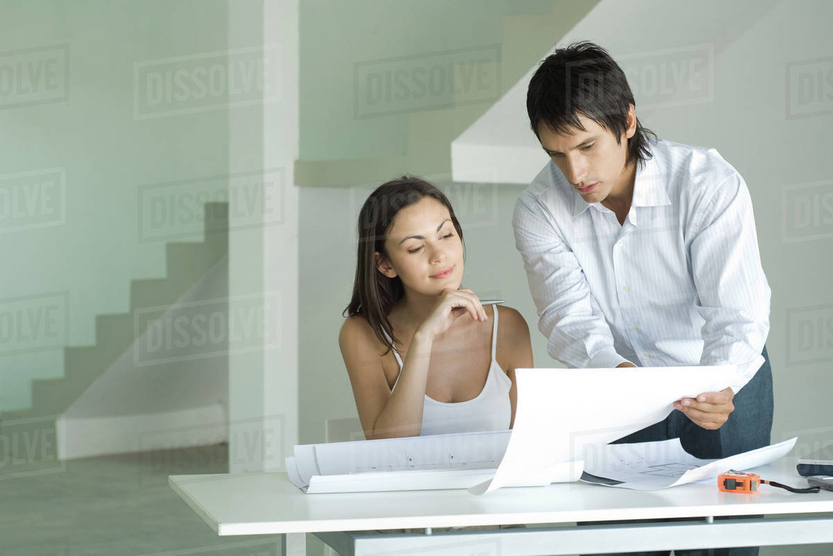 Couple looking at blueprints together, man leaning over table, holding ...