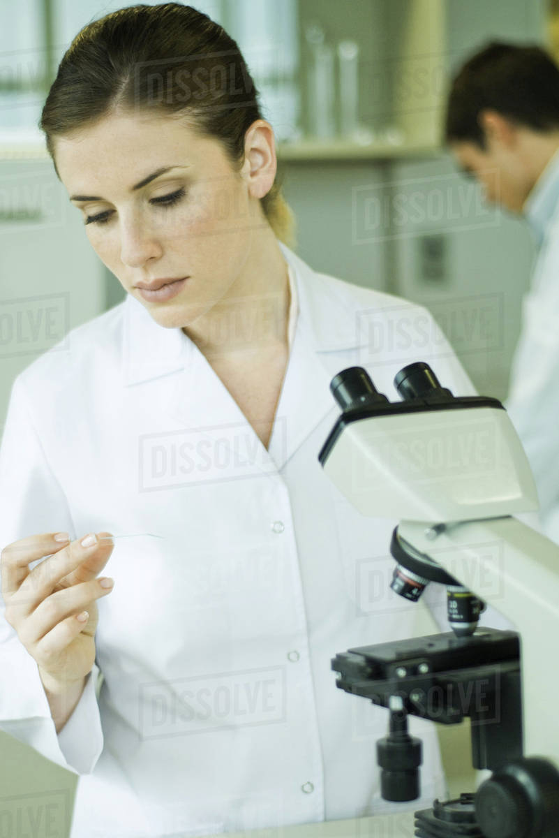 Female lab worker standing next to microscope, holding up and ...