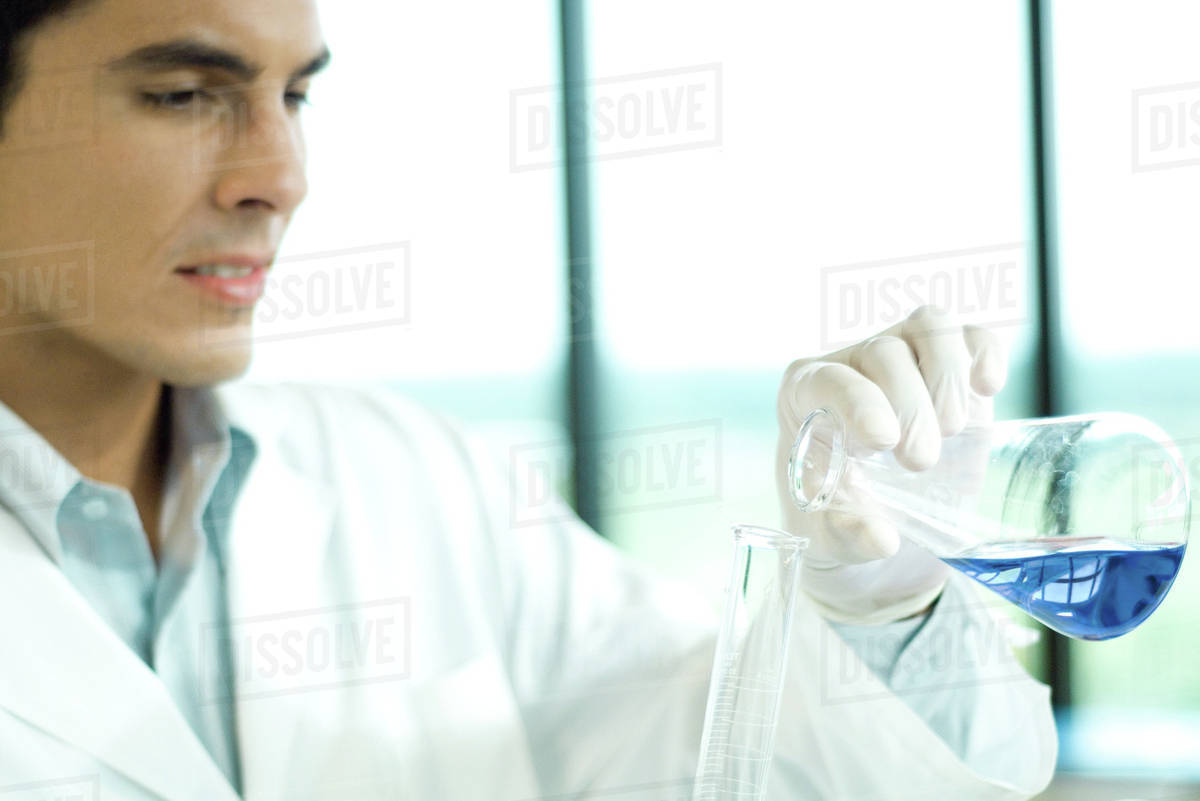 Male lab worker transferring solution from flask to graduated cylinder ...