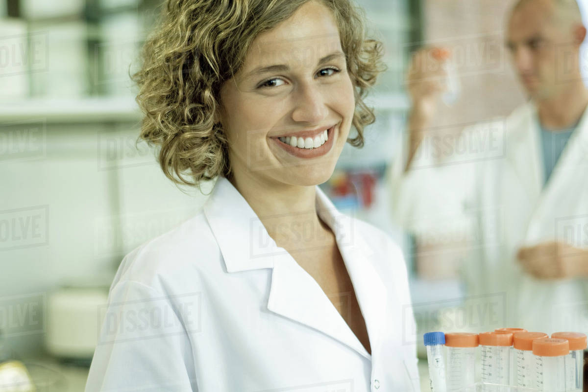 Female lab worker holding rack of empty test tubes, smiling at camera ...