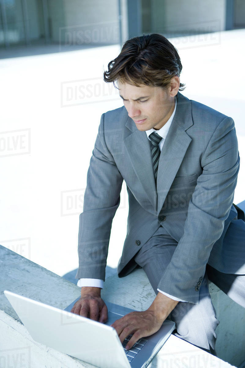 Young businessman sitting, using laptop computer, looking down ...
