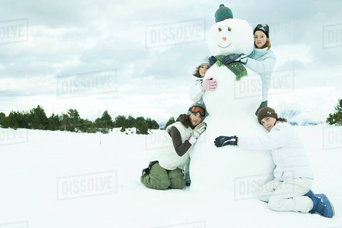 Four young friends embracing snowman, group portrait, one looking at ...