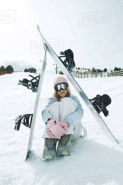 Preteen girl sitting on snow underneath propped up snowboards - Royalty ...