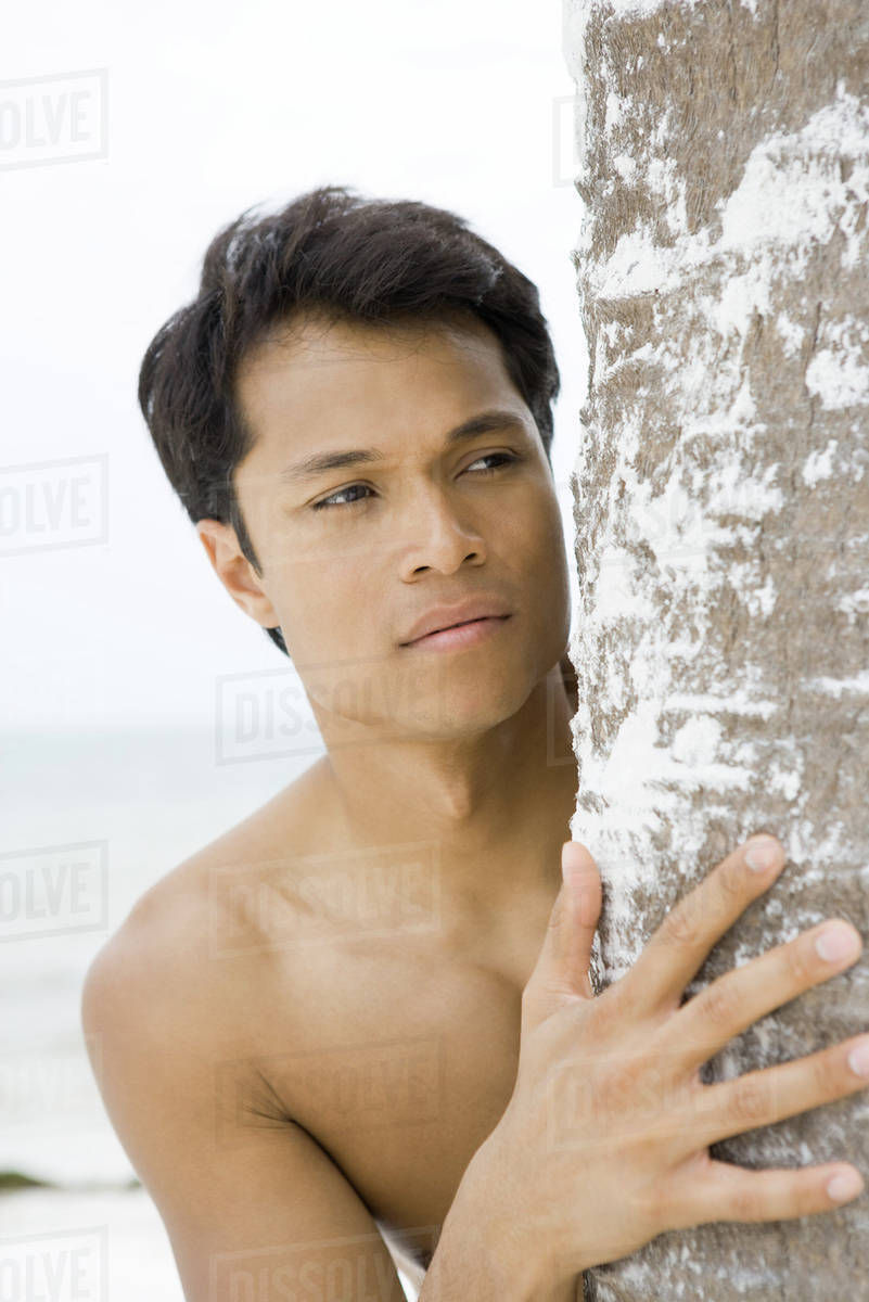 Barechested man looking around tree trunk, close-up - Royalty-free ...
